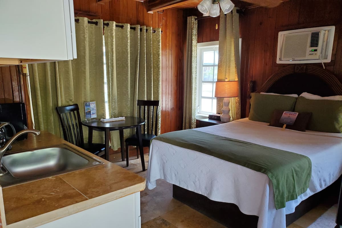 Um quarto com uma cama, escrivaninha, cadeira, pia e janela com cortinas.