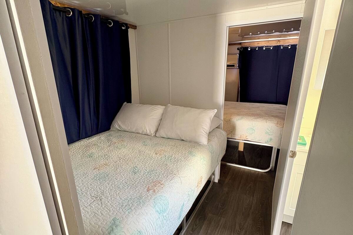 Quarto compacto com cama, uma mesinha e um banco.