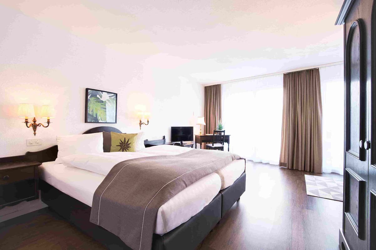 Quarto de hotel com cama grande, escrivaninha, televisão e guarda-roupa.