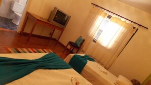 Quarto de hotel com duas camas, televisão, uma mesinha e janela com cortinas.