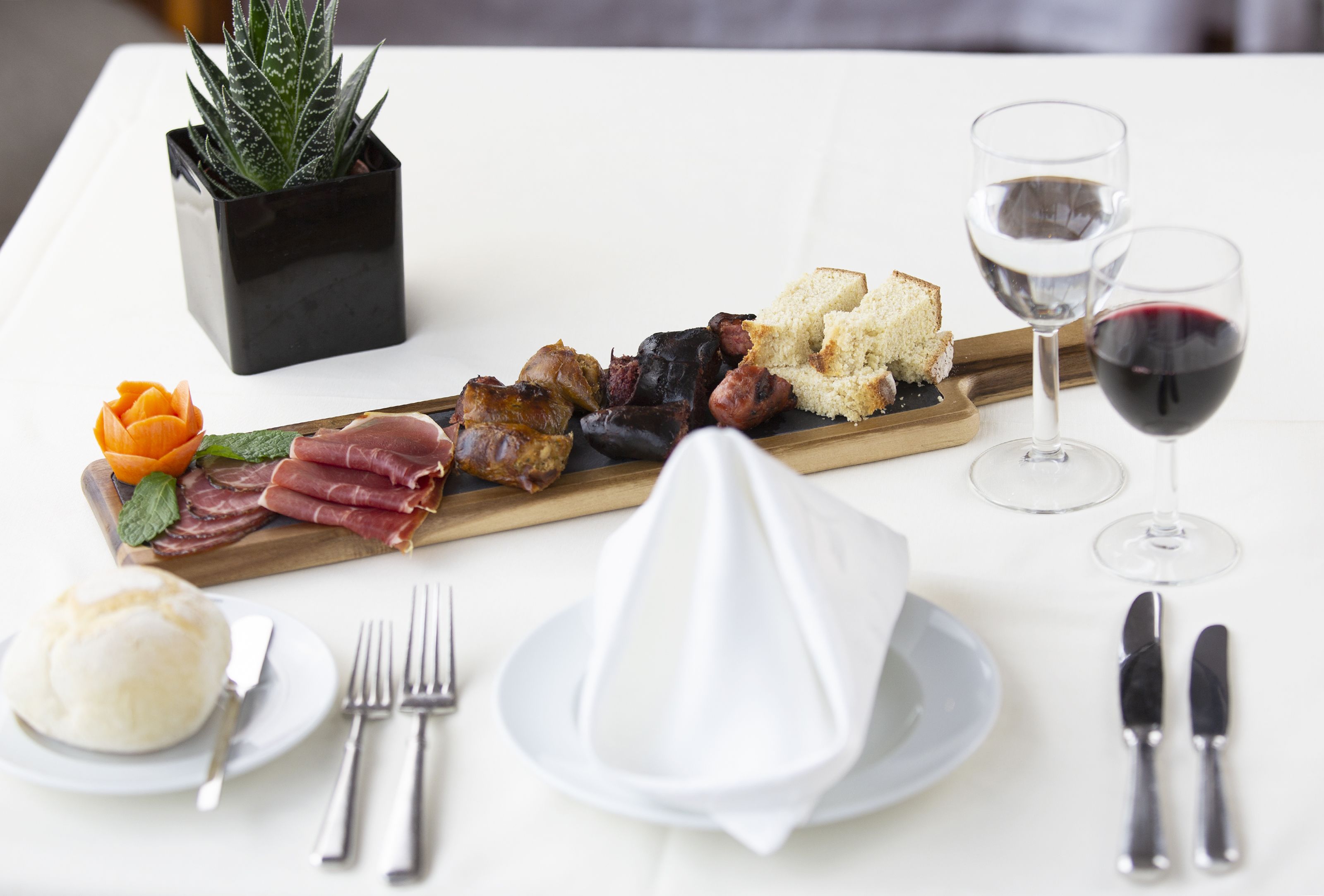 Uma mesa de jantar com tábua de frios, copos de vinho e um vaso de planta.