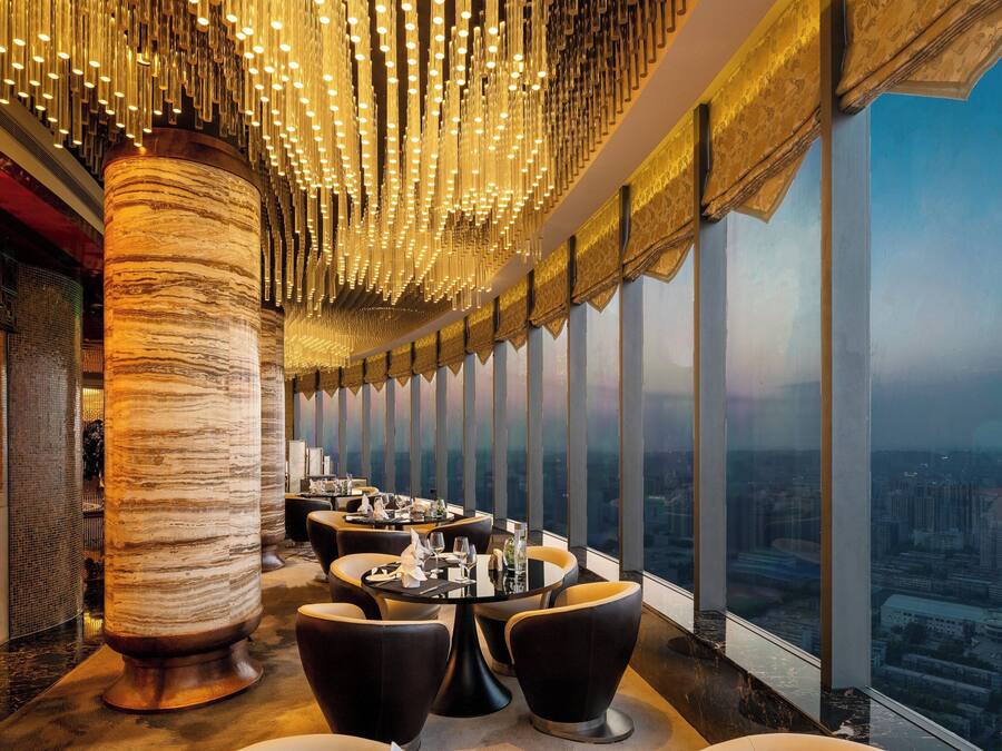 Restaurante em um arranha-céu com vista panorâmica da cidade, decoração moderna e uma luminária de teto singular.