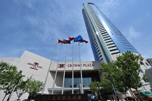 Um edifício moderno com a placa 'CROWNE PLAZA' e várias bandeiras em mastros.