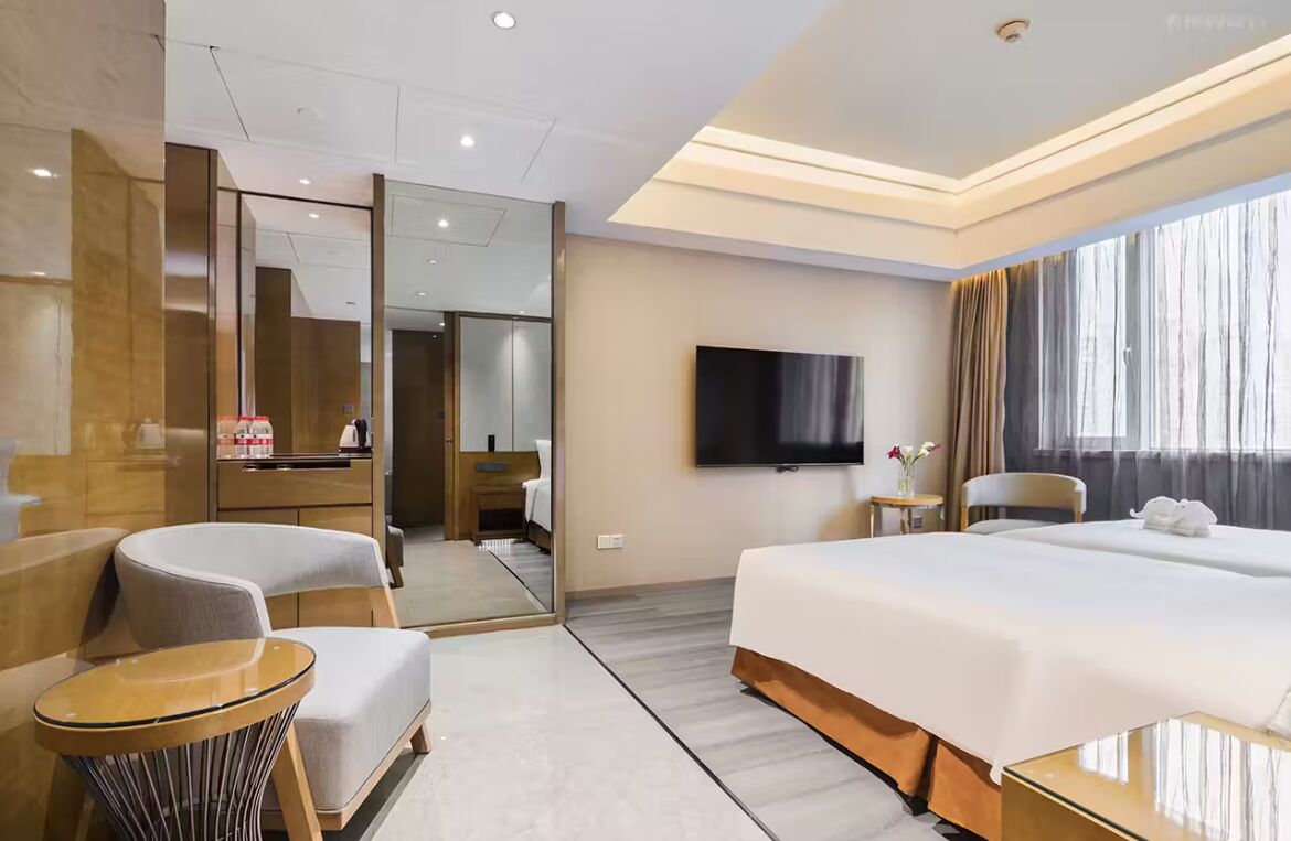 Quarto de hotel com uma cama grande, televisão, área de estar com cadeiras e uma mesa pequena.