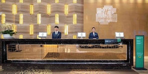Bancada de recepção de hotel com dois funcionários, placa da Holiday Inn e placa do IHG Rewards Club.