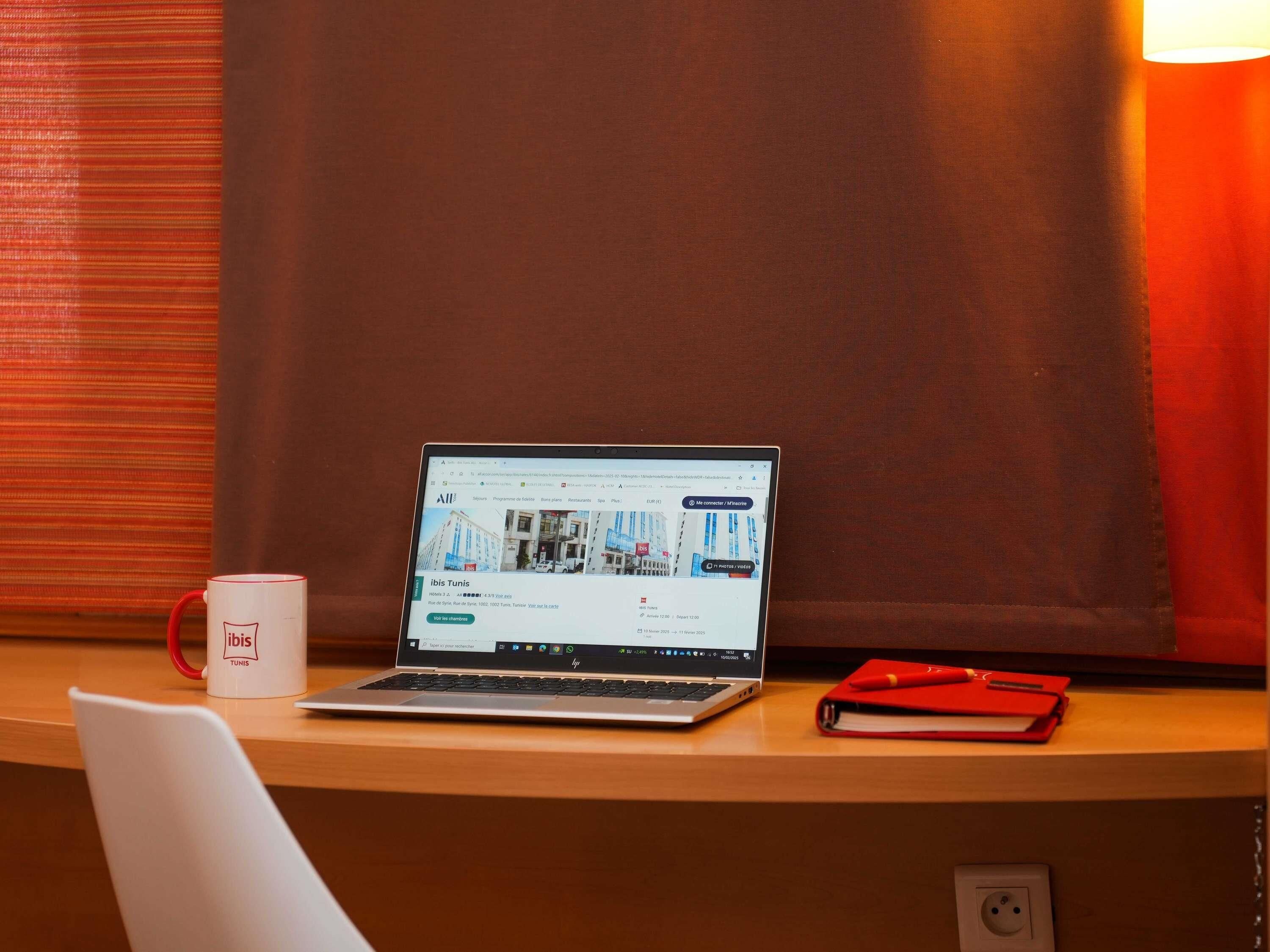 Um laptop sobre uma mesa, com uma caneca vermelha e um caderno vermelho.