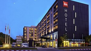 Um edifício moderno de hotel com vários andares, um logotipo de destaque da ibis e uma área de entrada bem iluminada.
