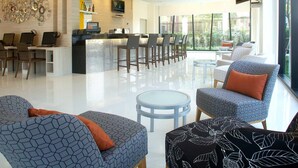 Um hall de hotel moderno com balcão de recepção, computadores, área de estar e janelas amplas.