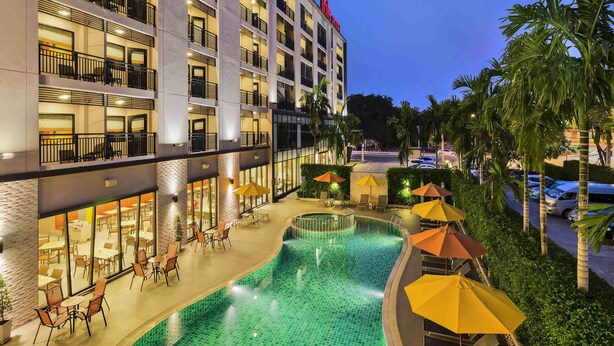 Hotel com piscina, área de estar externa e fachada bem iluminada.
