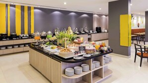 Um buffet de café da manhã com diversas opções de alimentos e bebidas, incluindo uma estação de café, e uma área de estar com mesas e cadeiras.