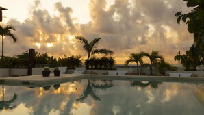 Piscina com reflexo nítido de palmeiras e céu ao pôr do sol.
