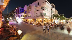 Restaurante com mesas ao ar livre, um letreiro com a inscrição 'EATITALY' e vista para a rua.