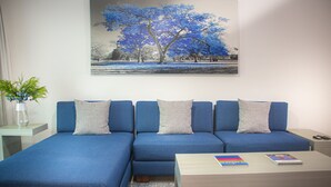 Uma sala de estar moderna com um sofá azul, uma mesa de centro e uma pintura de uma árvore.