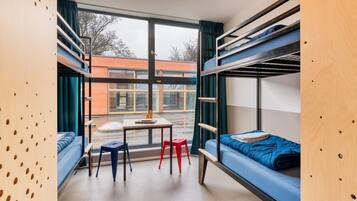 Um dormitório com beliches, uma mesa pequena e uma janela com cortinas.