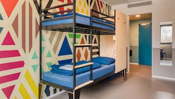 Quarto com beliche, parede com padrão geométrico, porta de madeira e vista para um corredor.