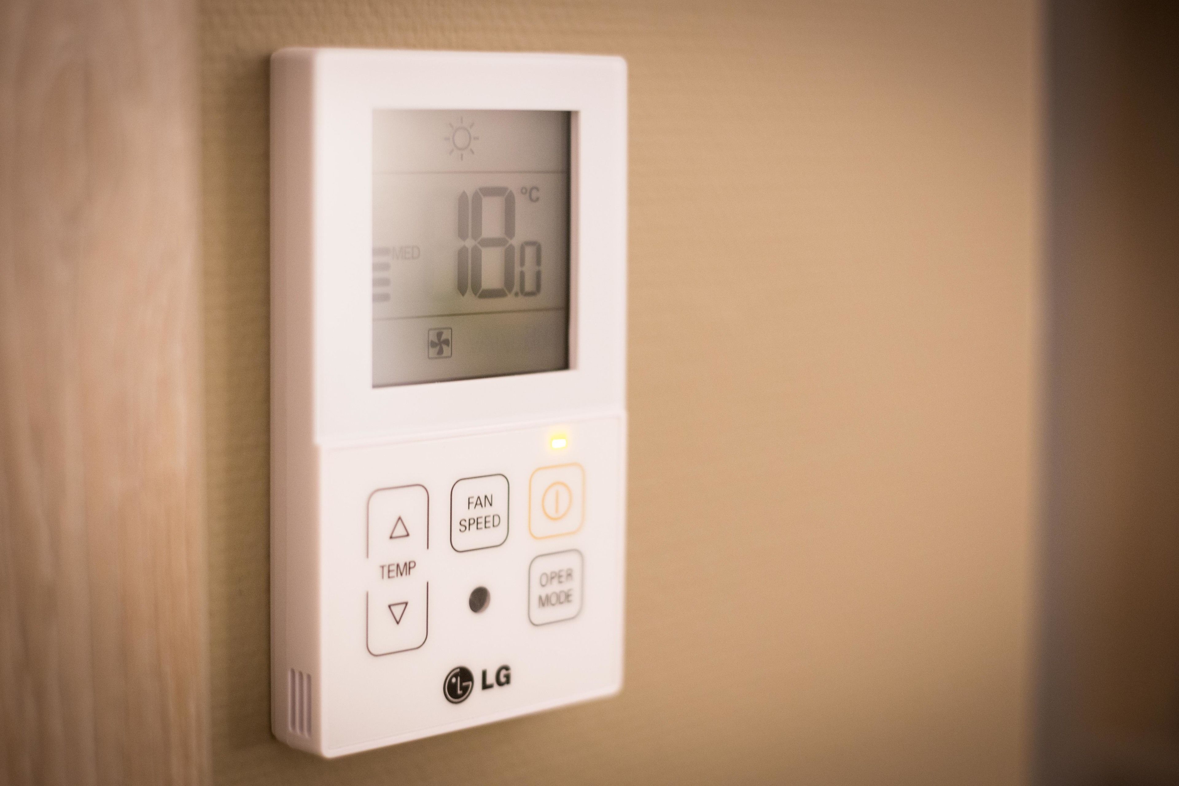 Um termostato branco da LG com visor digital mostrando 18°C, botões de controle de temperatura e controle de velocidade do ventilador.