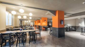 Uma cafeteria ampla com várias mesas e cadeiras, com design moderno e detalhes em laranja, além de teto alto com iluminação pendente.
