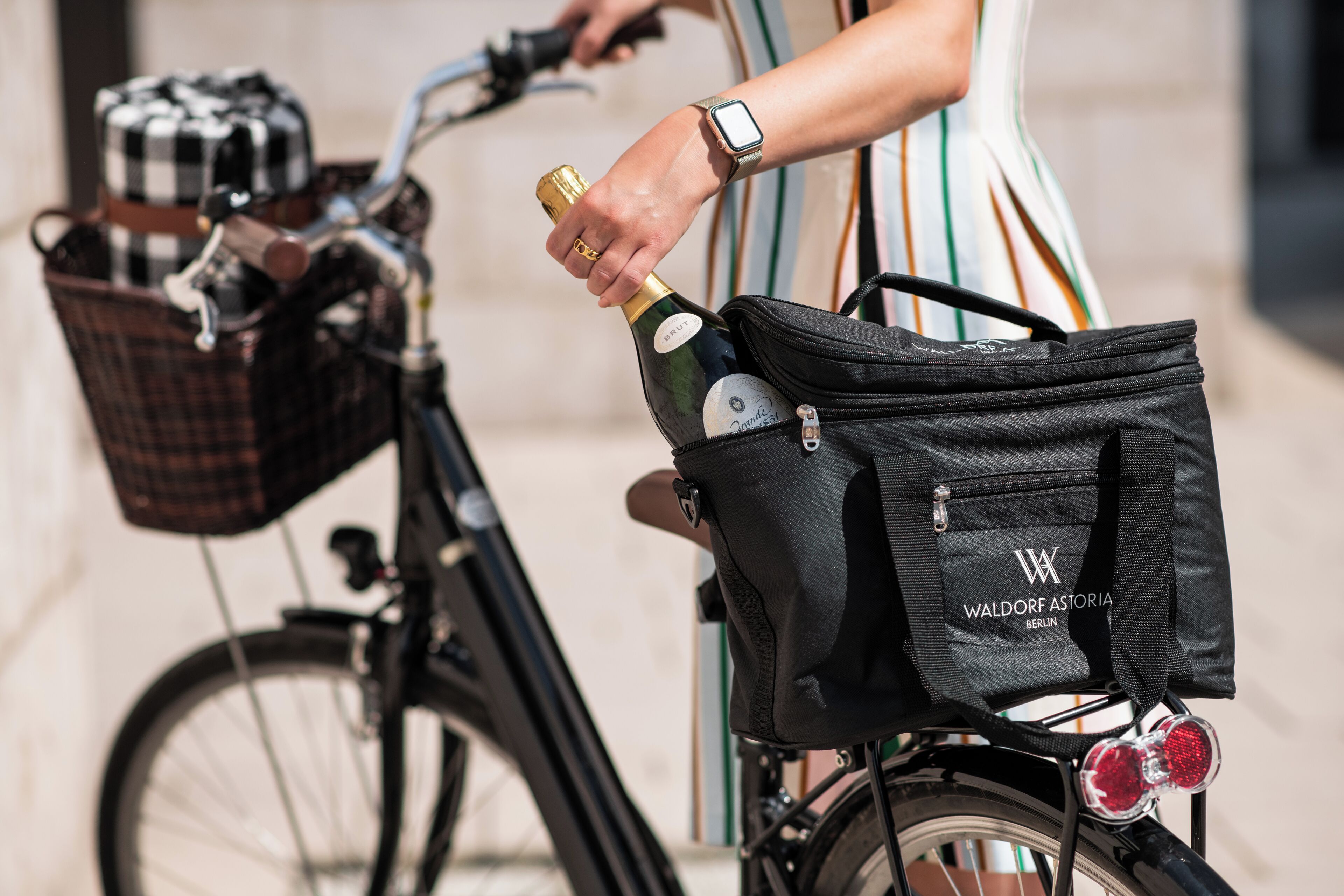 Uma bicicleta com uma cesta e uma bolsa preta com logotipo.