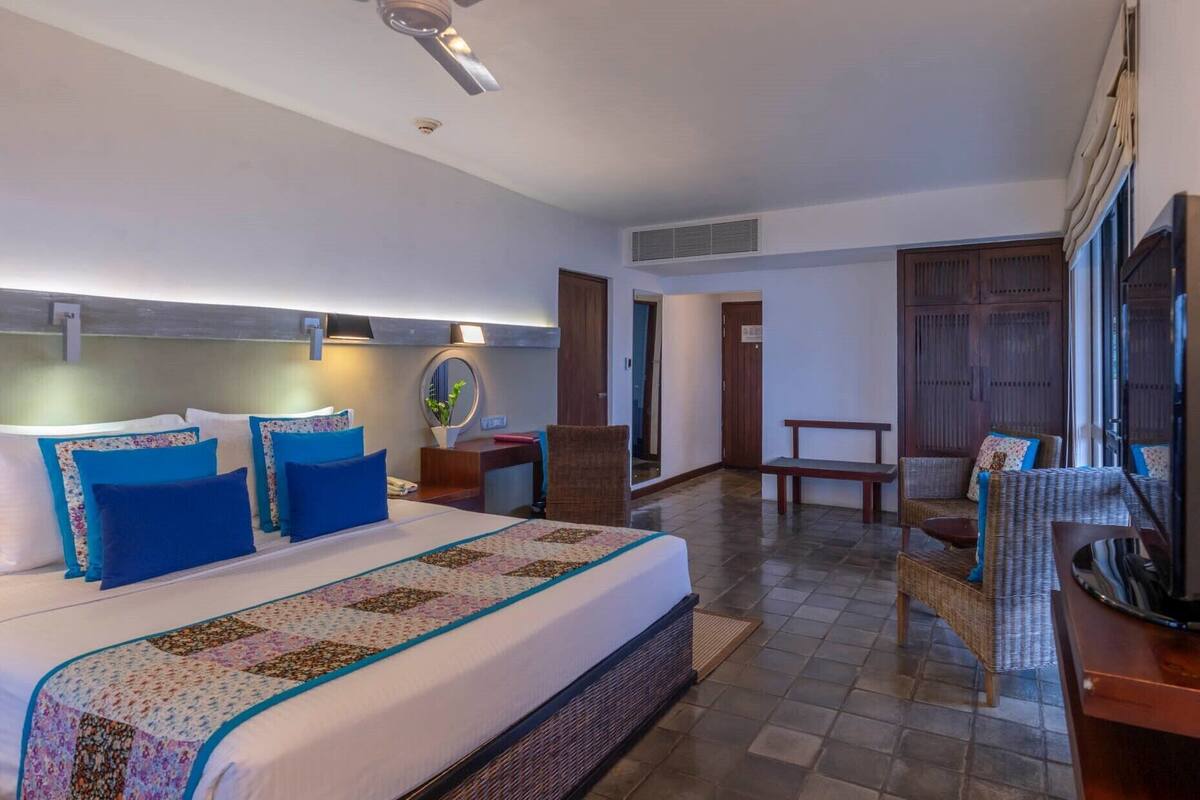 Quarto de hotel com uma cama grande, uma escrivaninha, uma cadeira, uma televisão e um banheiro visível através de uma porta aberta.