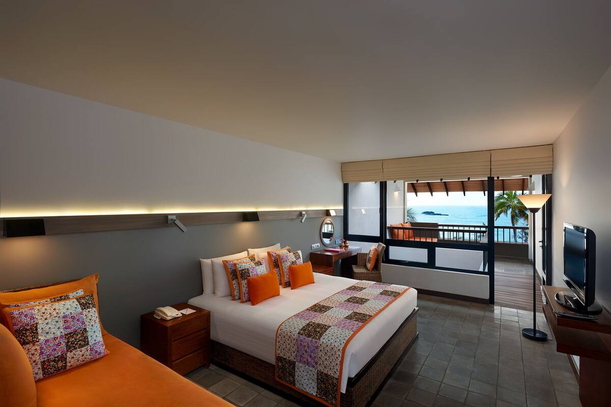 Quarto de hotel moderno com uma cama grande, uma escrivaninha e varanda com vista para o mar.