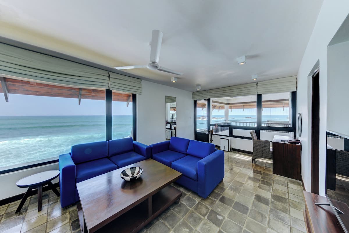 Quarto moderno com sofá azul, uma pequena mesa e vista para o oceano.