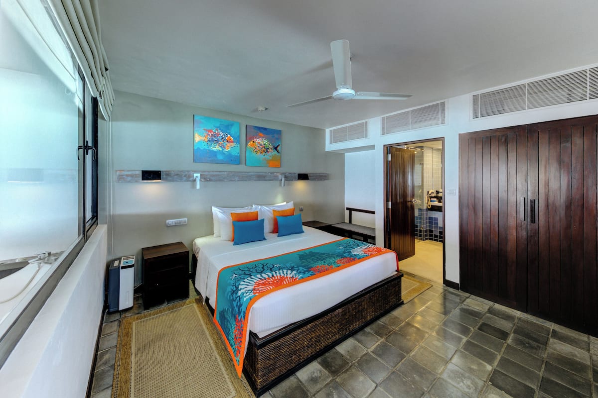 Quarto de hotel com cama, ventoinha no teto, obras de arte na parede e vista para o banheiro.