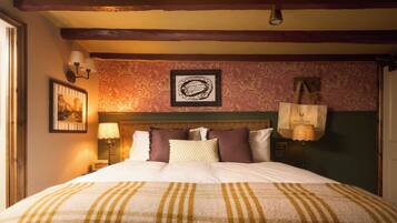 Quarto de hotel com uma cama grande, cabeceira, quadro emoldurado, abajur e parede com papel de parede estampado.