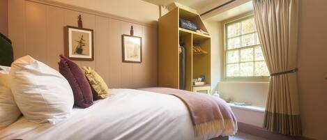 Quarto com cama, guarda-roupa, janela com cortinas e prateleira fixada na parede com objetos.