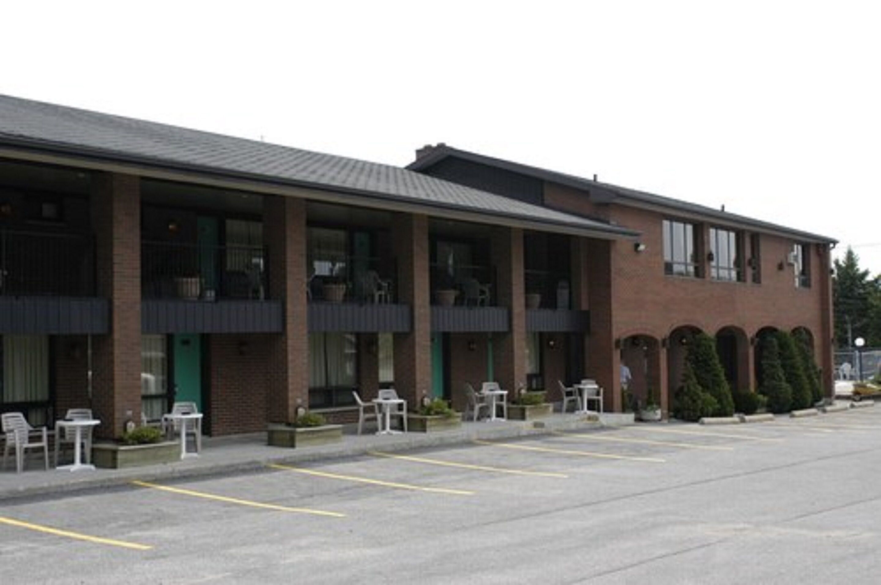 Um motel com uma fileira de quartos, uma área de estar coberta ao ar livre e um estacionamento.