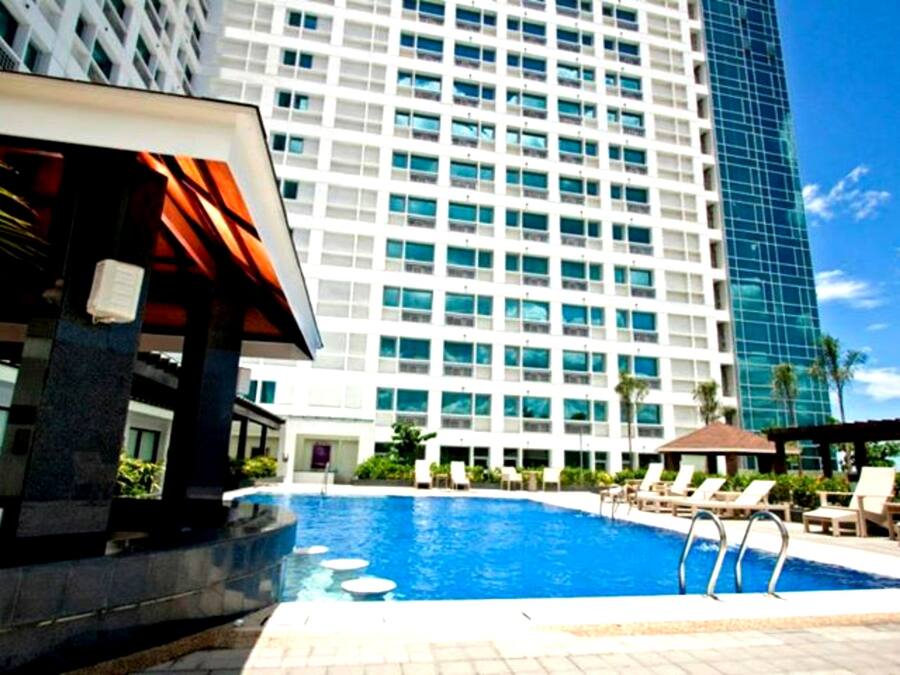Piscina com espreguiçadeiras e um edifício moderno com fachada de vidro ao fundo.