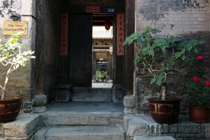 Entrada de um edifício tradicional, com degraus que levam a uma porta. Placas indicam a localização e há um vaso de planta nos degraus.
