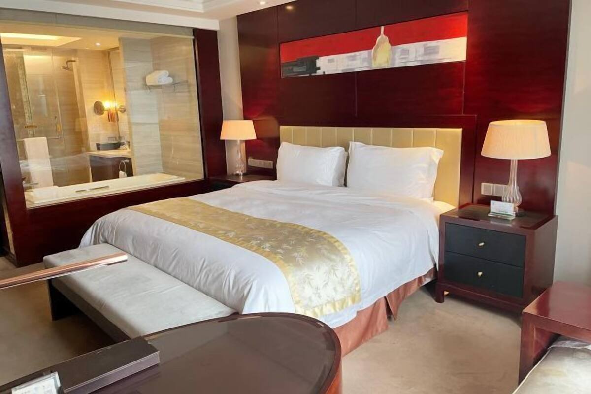 Quarto de hotel com uma cama grande, mesas de cabeceira, um espelho e vista para o banheiro.