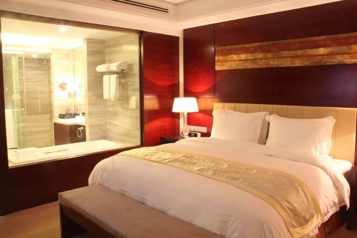 Quarto de hotel com uma cama grande, mesa de cabeceira, espelho e vista para o banheiro.