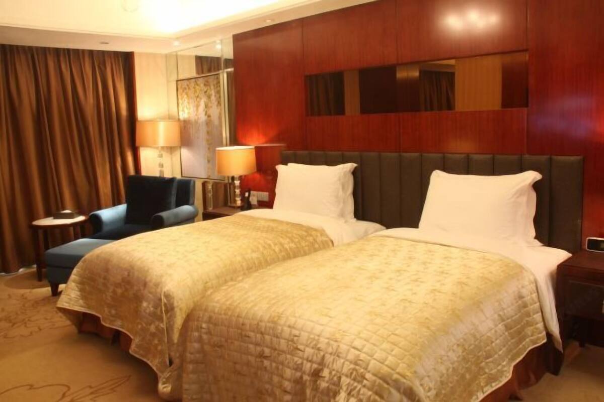 Quarto de hotel com duas camas, uma escrivaninha, uma cadeira e um espelho grande.