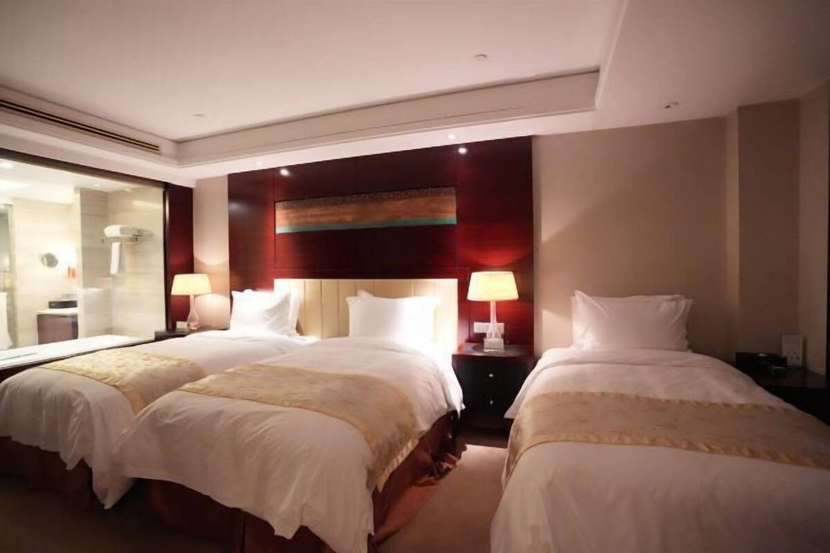 Quarto de hotel com duas camas, um espelho grande, um quadro na parede e uma mesa de cabeceira com abajur.
