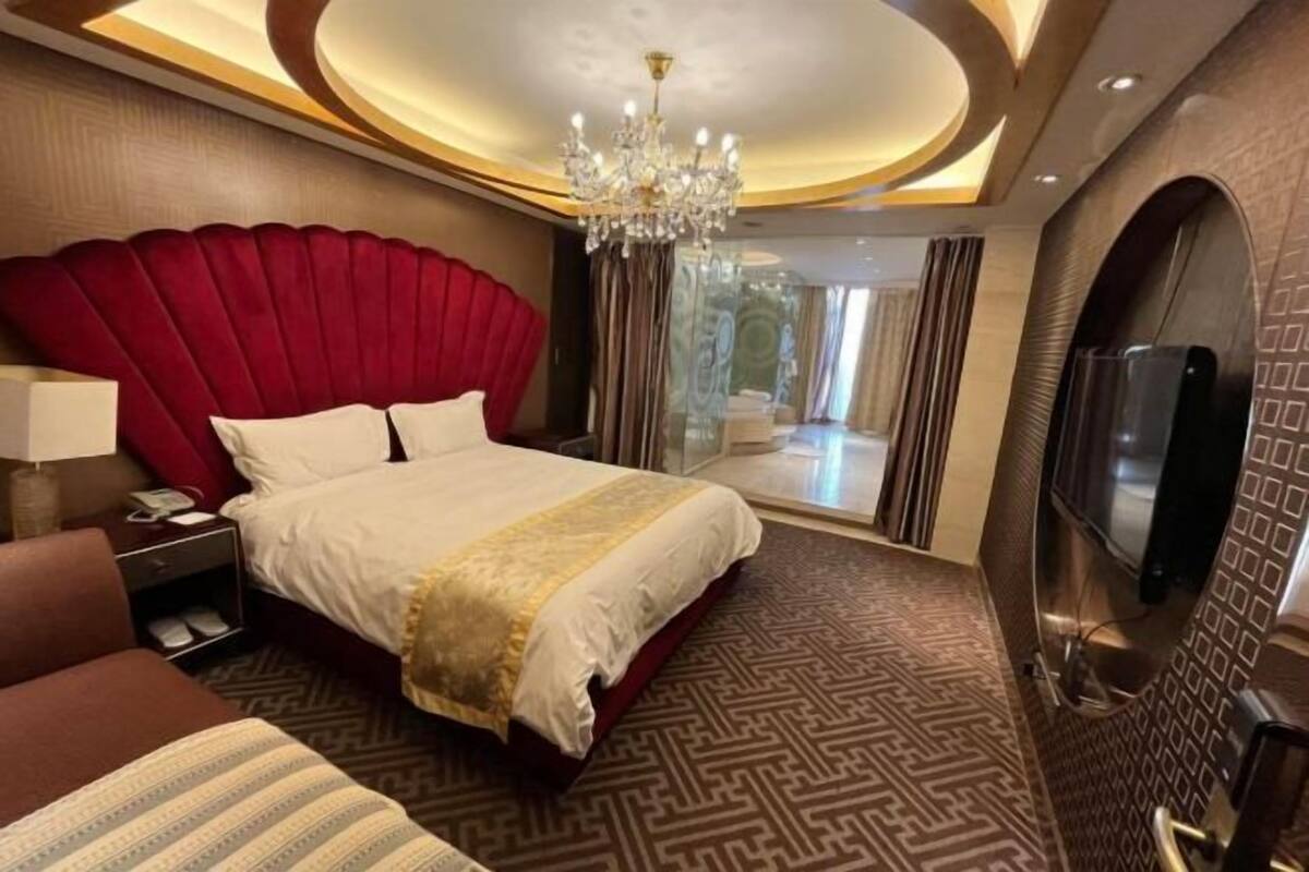Quarto de hotel com uma cama grande, um candelabro, uma TV e vista para o exterior.