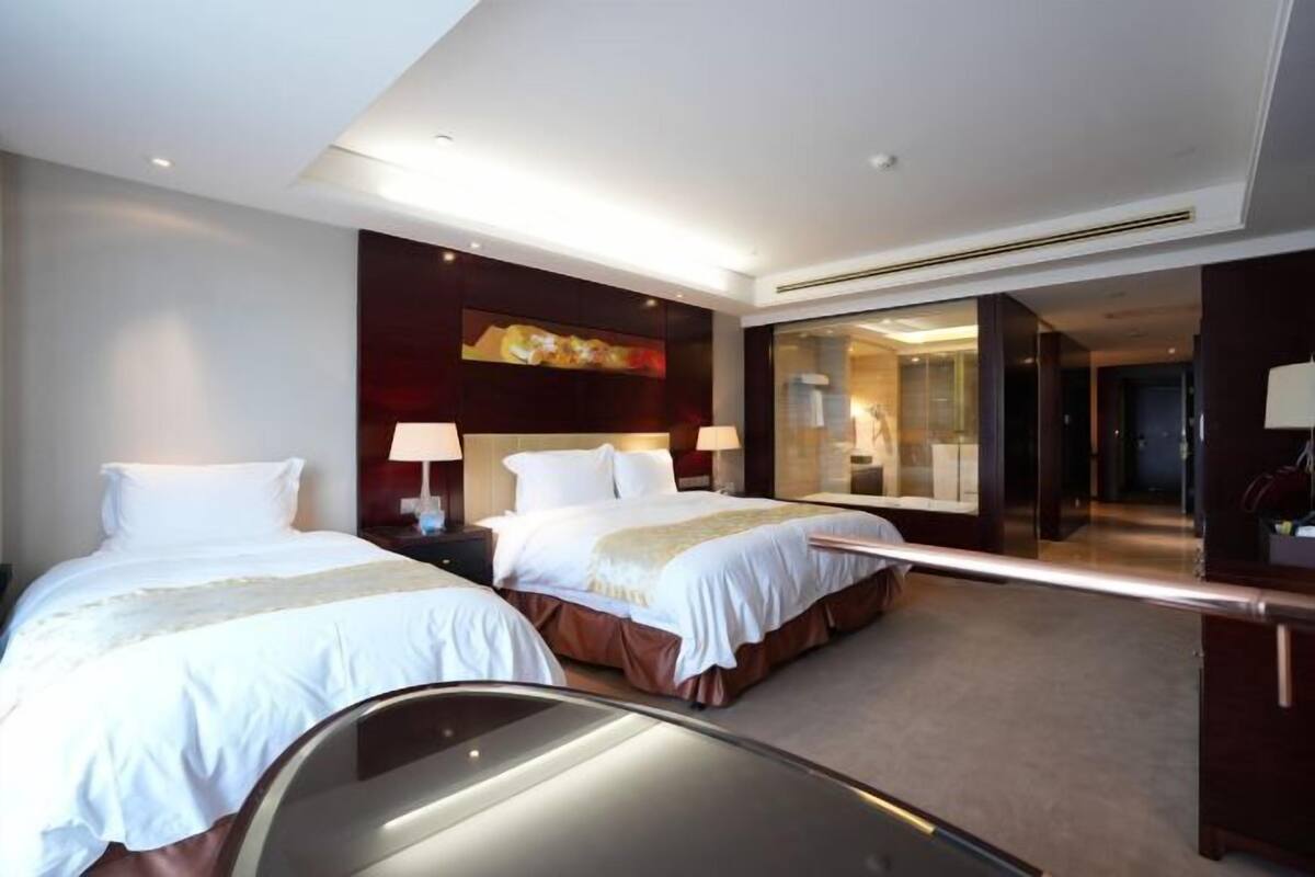 Quarto de hotel com duas camas, um espelho grande e um painel de vidro.