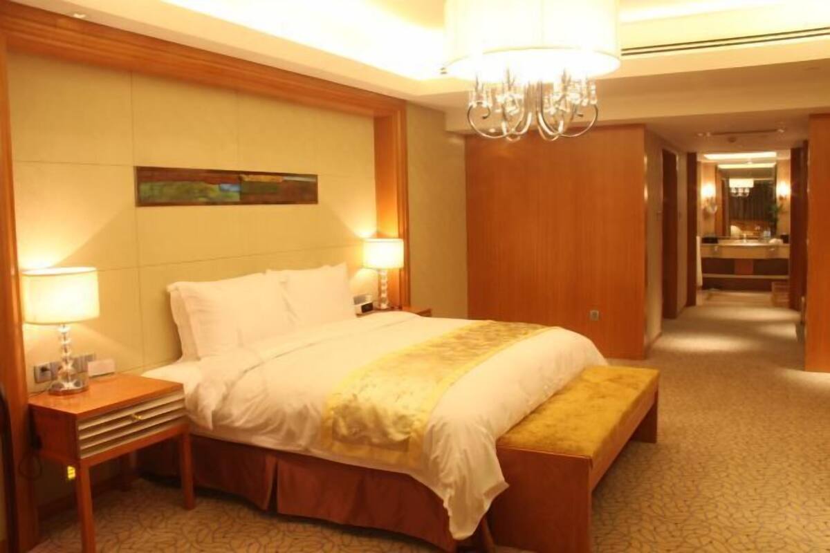 Quarto de hotel com cama grande, abajures, um banco, um candelabro e um quadro na parede.