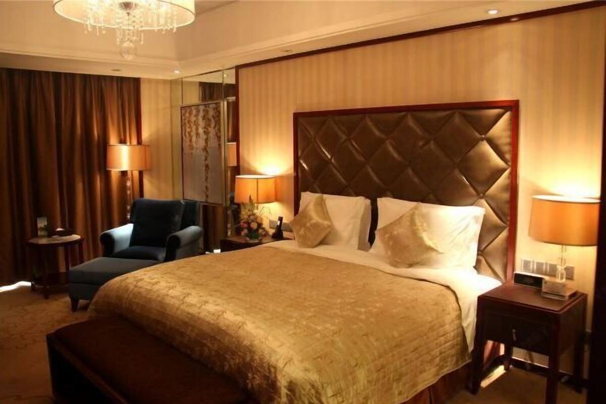 Quarto de hotel com uma cama grande, uma cadeira, uma mesa de cabeceira e um candelabro.