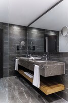Uma casa de banho moderna com lavatório de mármore, um espelho grande e uma prateleira de madeira.