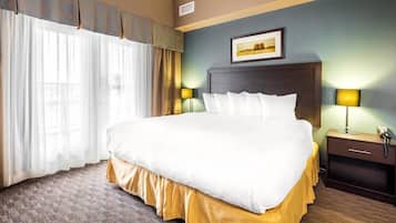 Quarto de hotel com uma cama grande, uma mesinha de cabeceira com abajur e um quadro na parede.