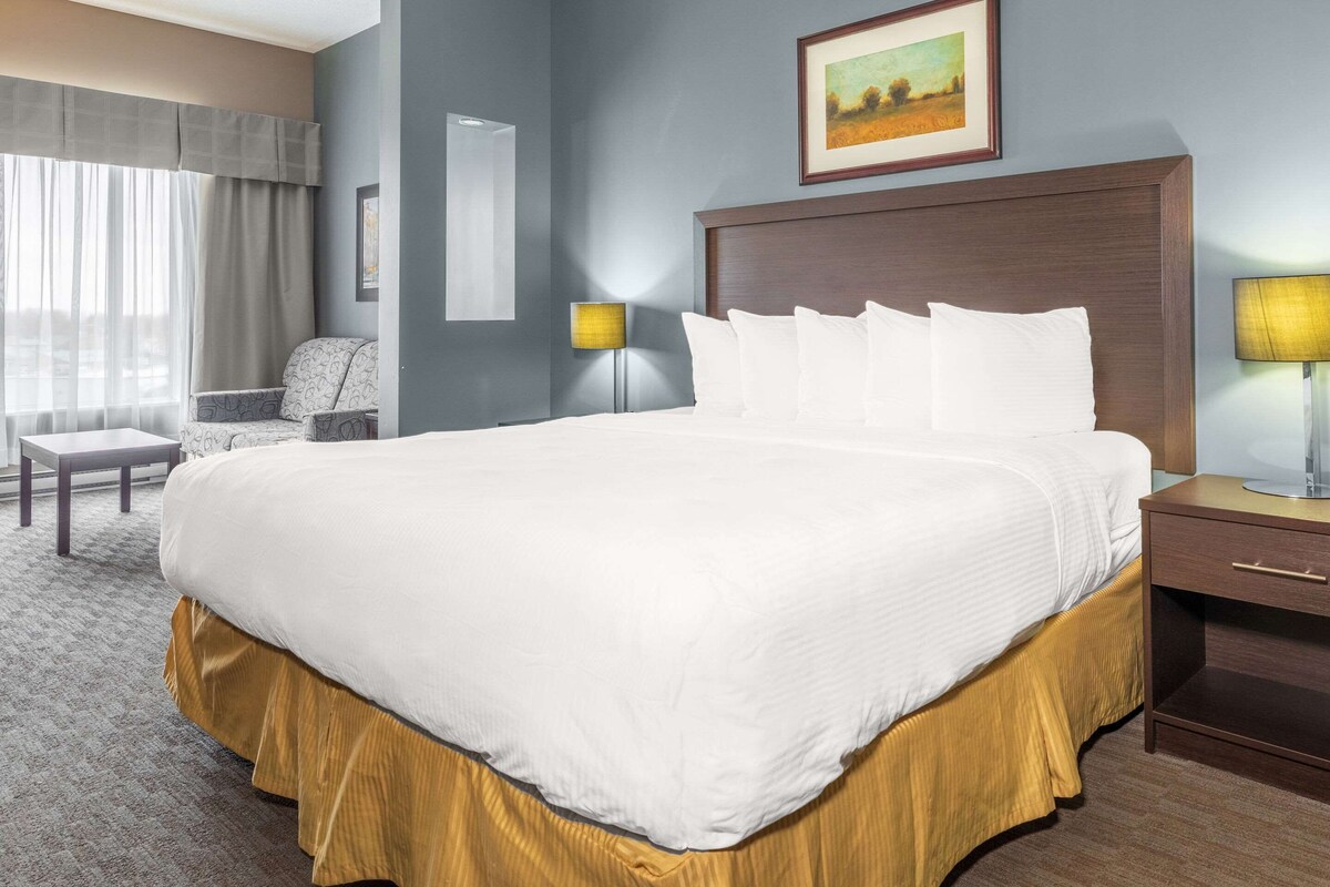 Quarto de hotel com uma cama grande, uma cadeira, uma mesa de cabeceira e um abajur.
