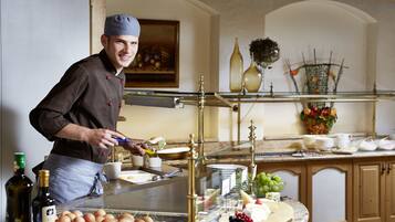 Um chef preparando comida em uma cozinha com bancada de mármore, vitrine de vidro e diversos utensílios de cozinha.