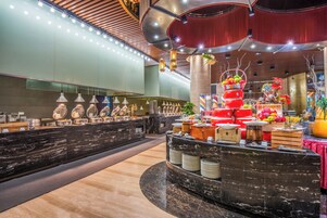 Uma área de buffet com diversas opções de comida, um balcão de mármore e uma composição decorativa de frutas.