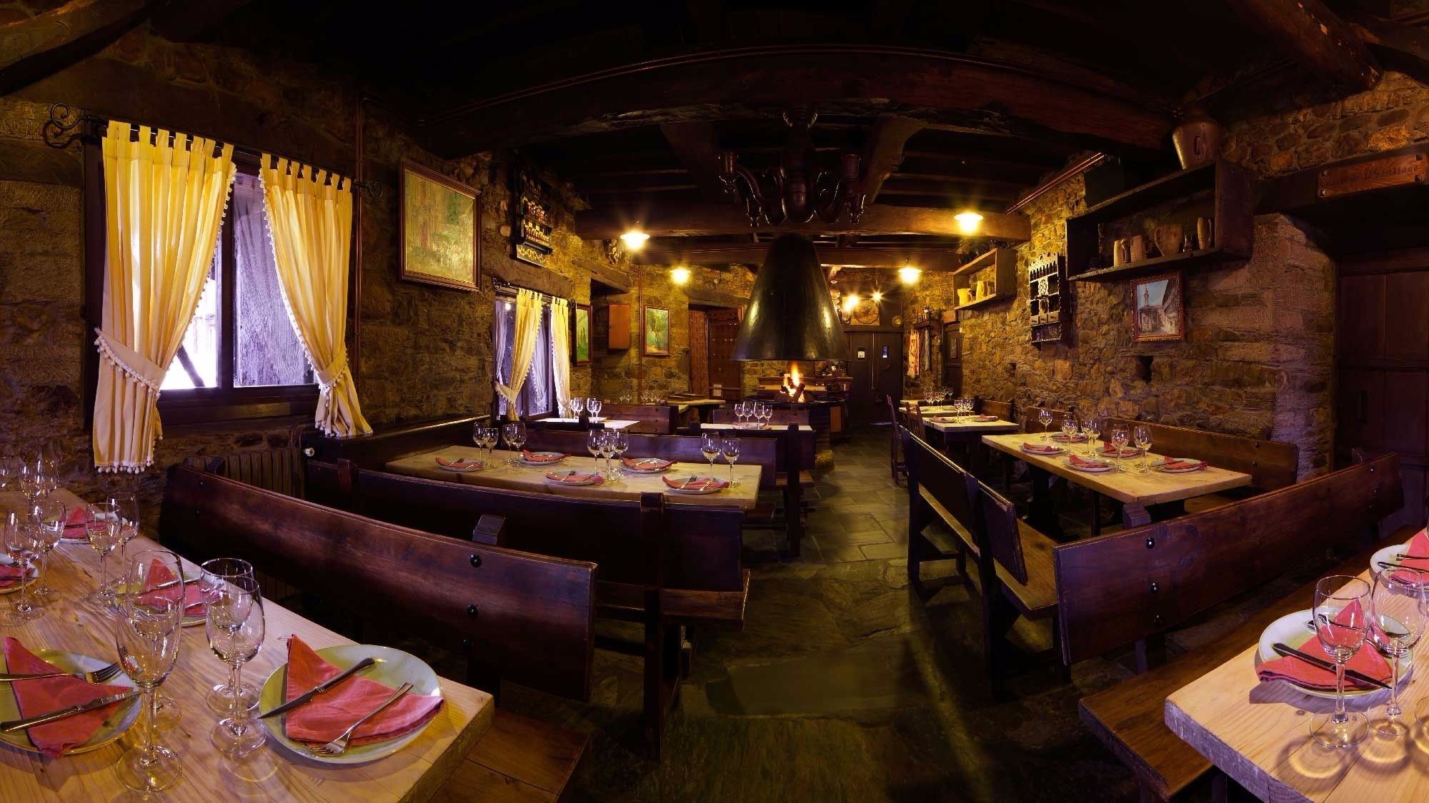 Um restaurante com mesas e bancos de madeira, paredes de pedra e luminárias pendentes.