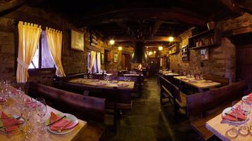 Um restaurante com mesas e bancos de madeira, paredes de pedra e luminárias pendentes.