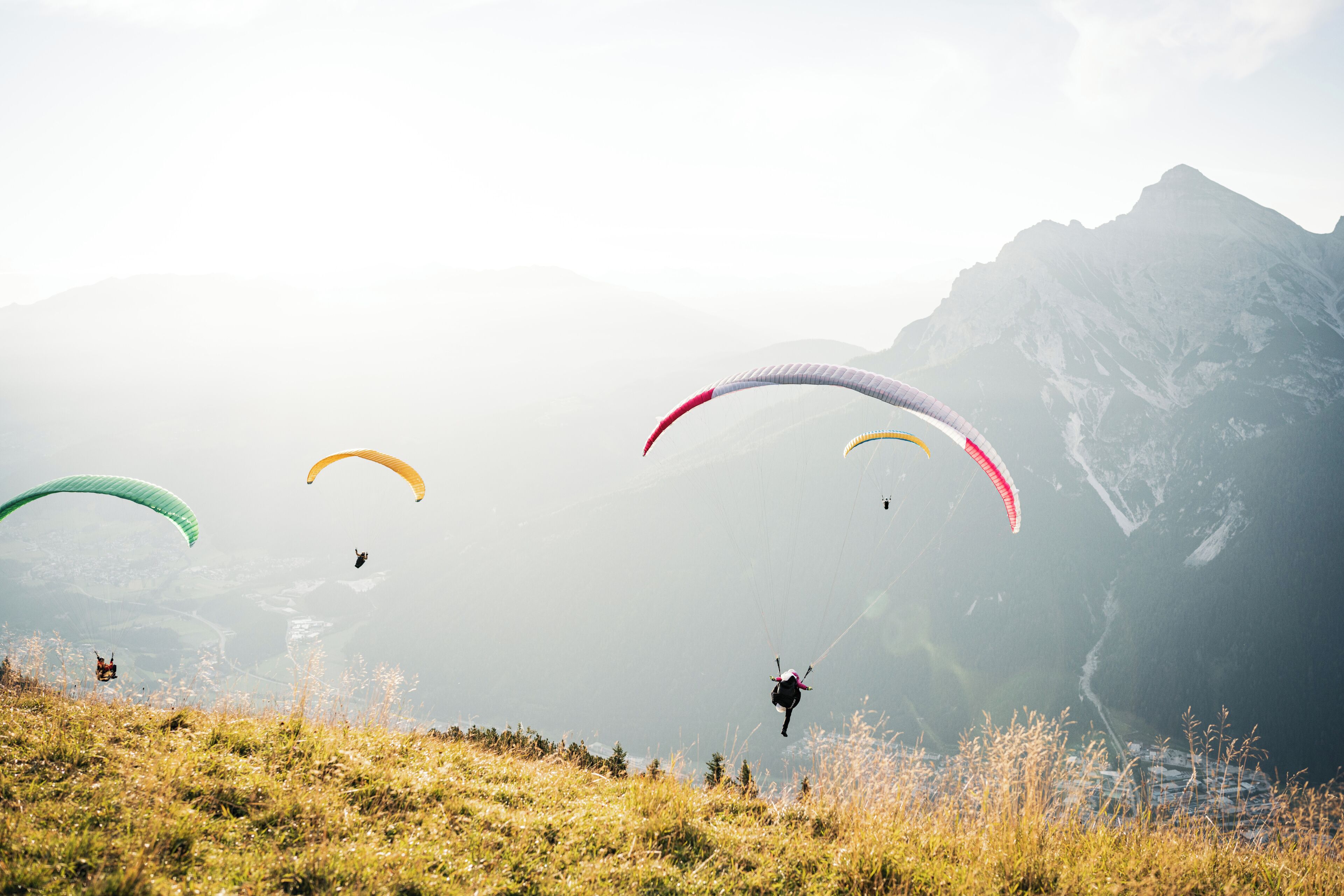 Paisagem montanhosa com quatro parapentes no ar.