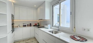 Cozinha moderna com armários brancos, uma pia de aço inoxidável e uma janela que permite entrada de luz natural.