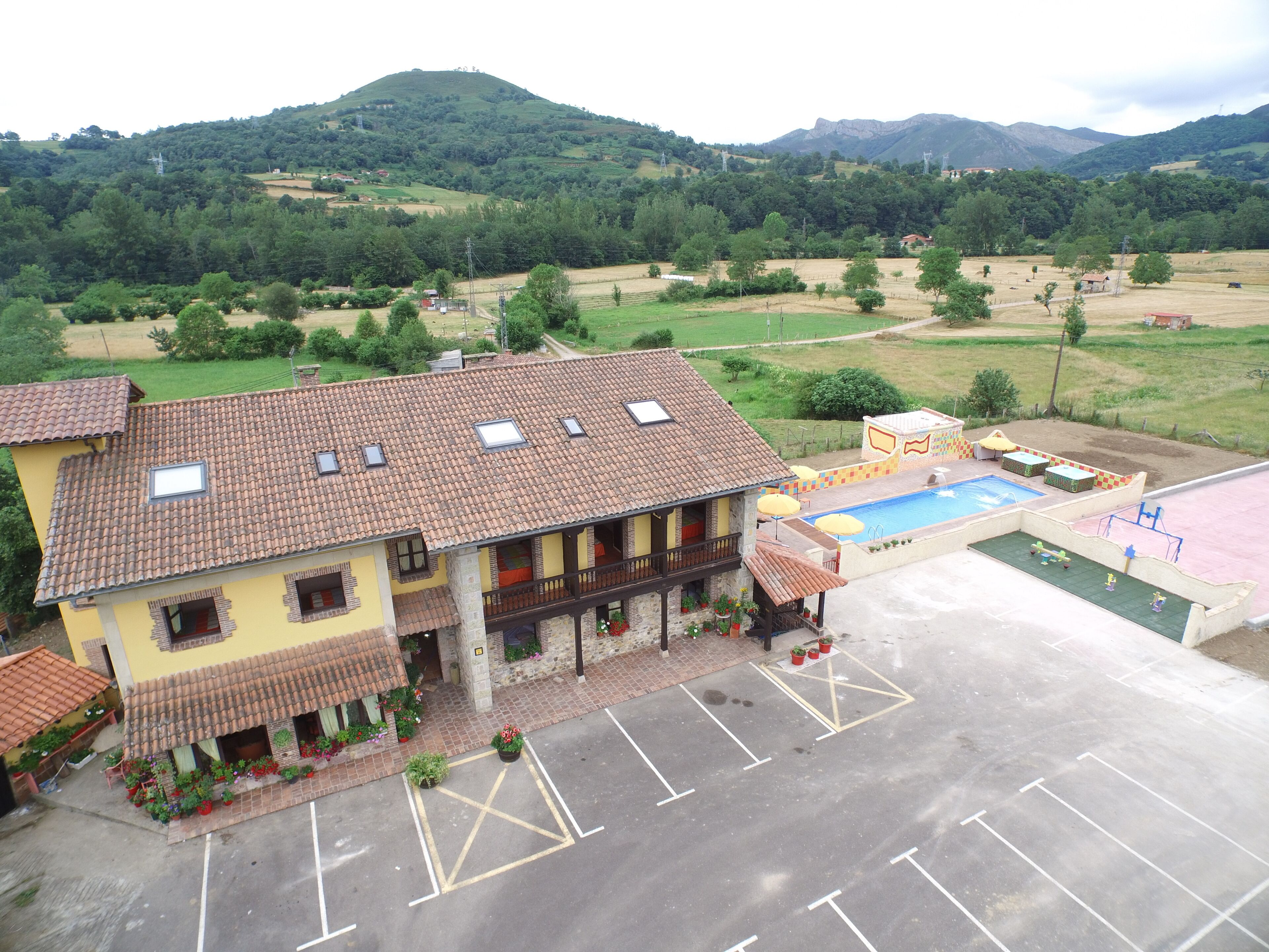 Um edifício de dois andares com telhado de telhas, piscina e estacionamento.