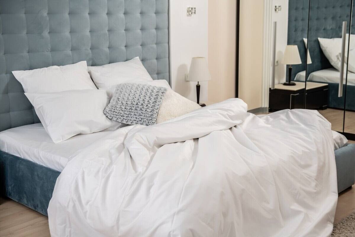 Cama bem arrumada com roupa de cama branca e cabeceira azul.
